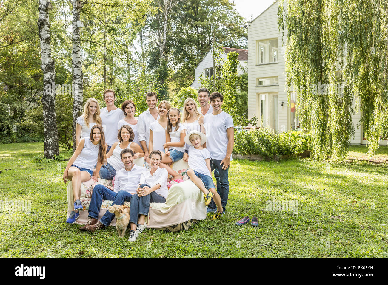 Portrait of group of people sitting on, and standing around sofa, in ...