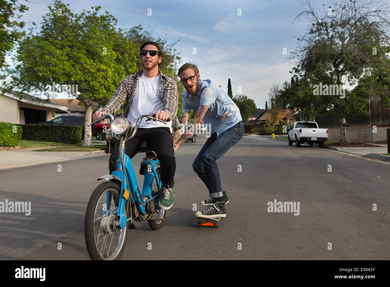 Male skateboarder skitching on friends moped on suburban road Stock ...