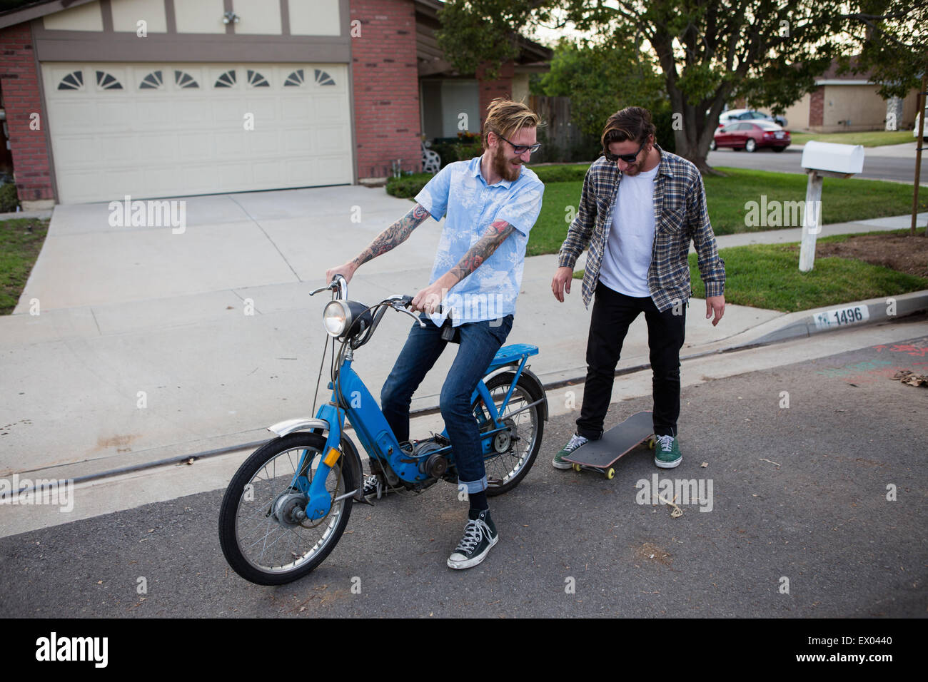 Male skateboarder preparing to skitch on friends moped on suburban road ...