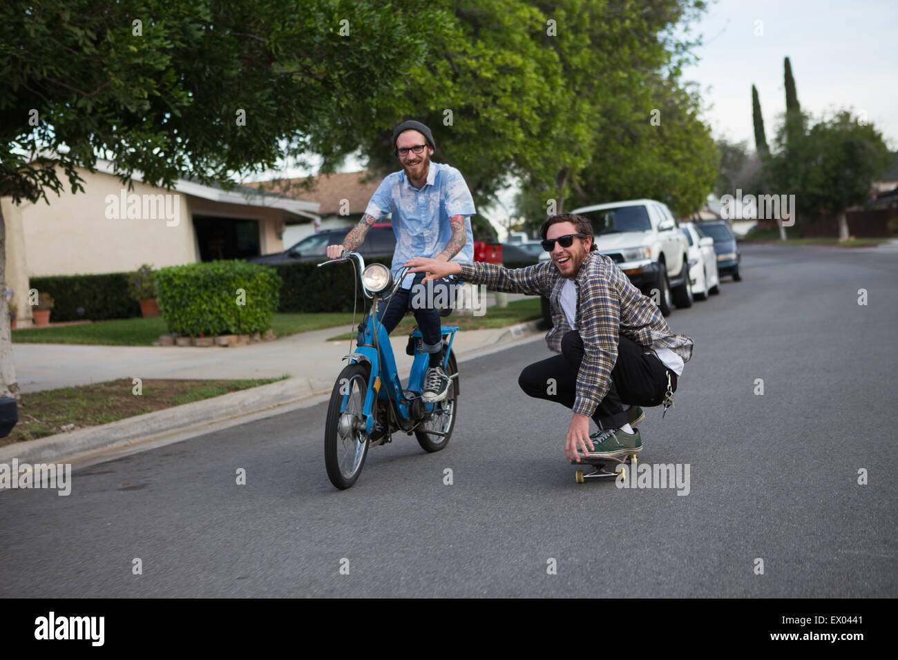 Male skateboarder skitching on friends moped along suburban road Stock ...