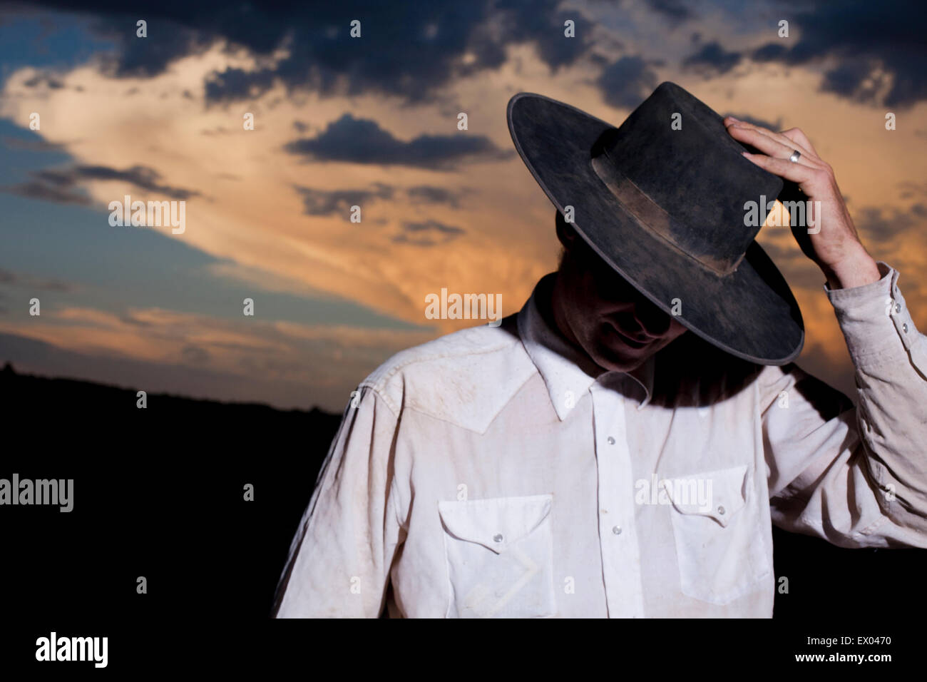 Portrait of cowboy shading face with stetson at sunset, Nevada, USA ...