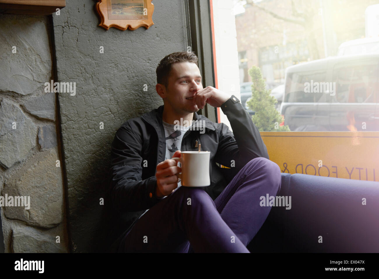 Young man sitting in cafe window seat looking out of window Stock Photo ...