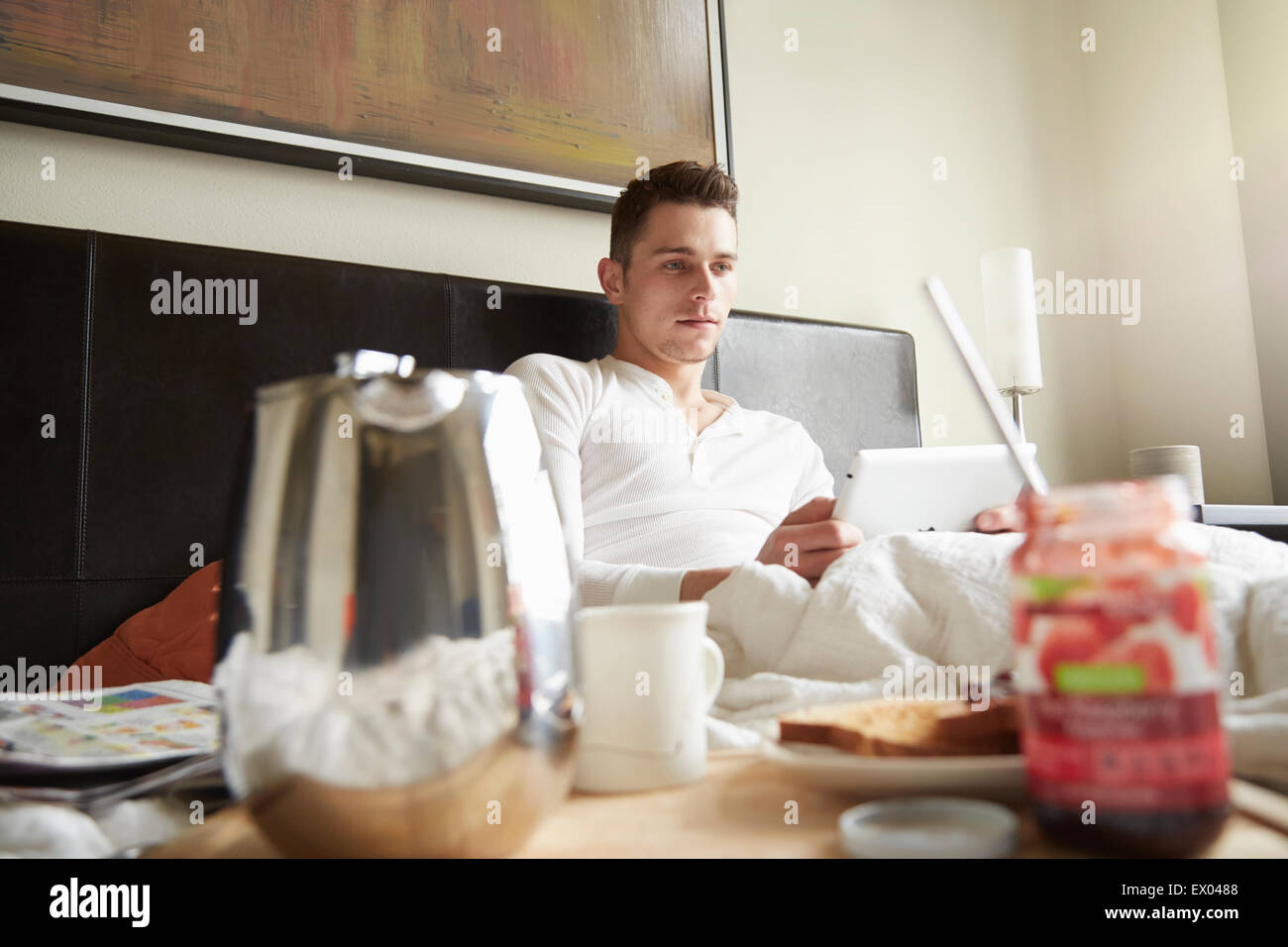 Young man sitting up in bed reading digital tablet Stock Photo - Alamy