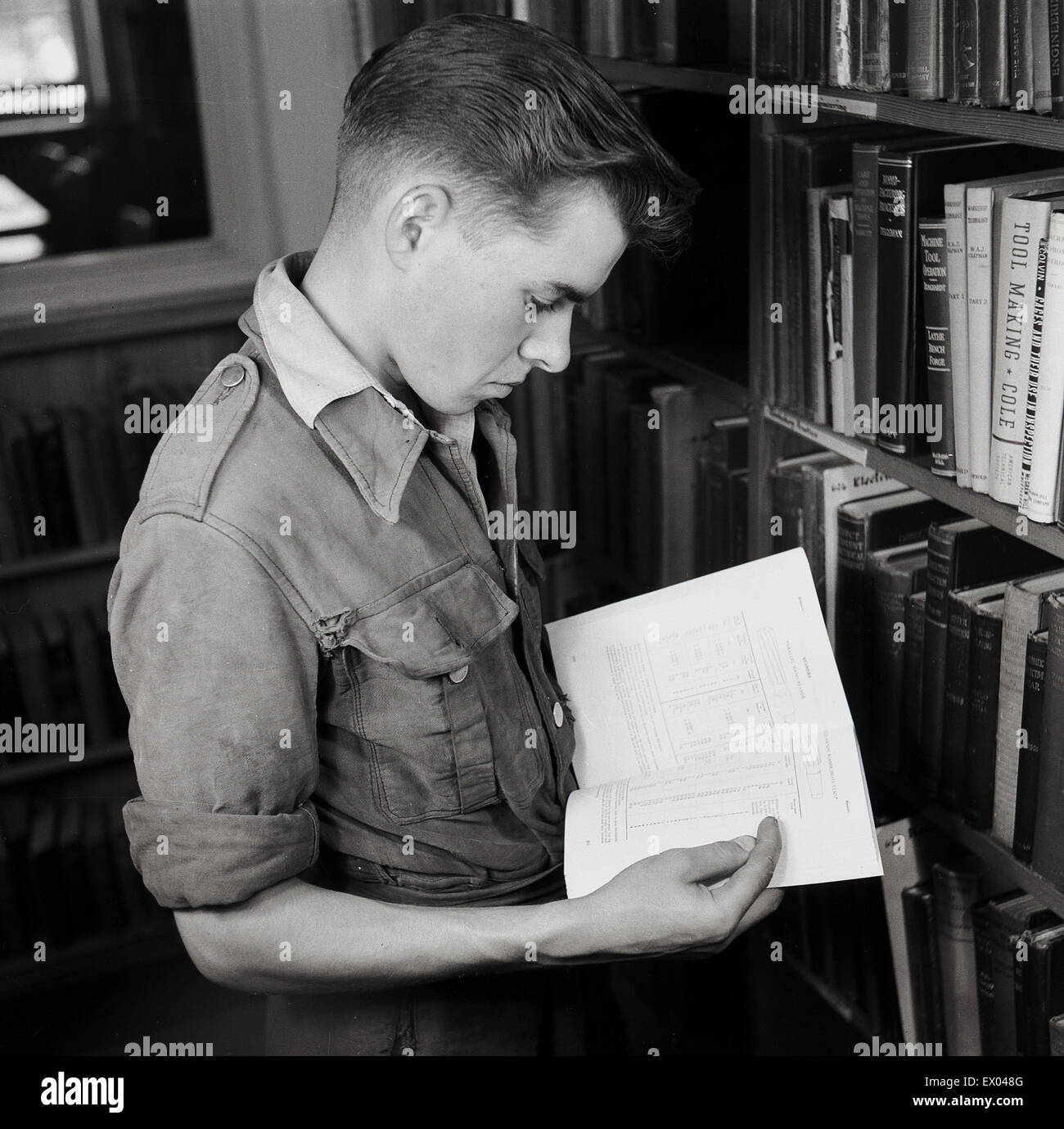 Historical, 1950s, picture shows a young man in a library studying a ...
