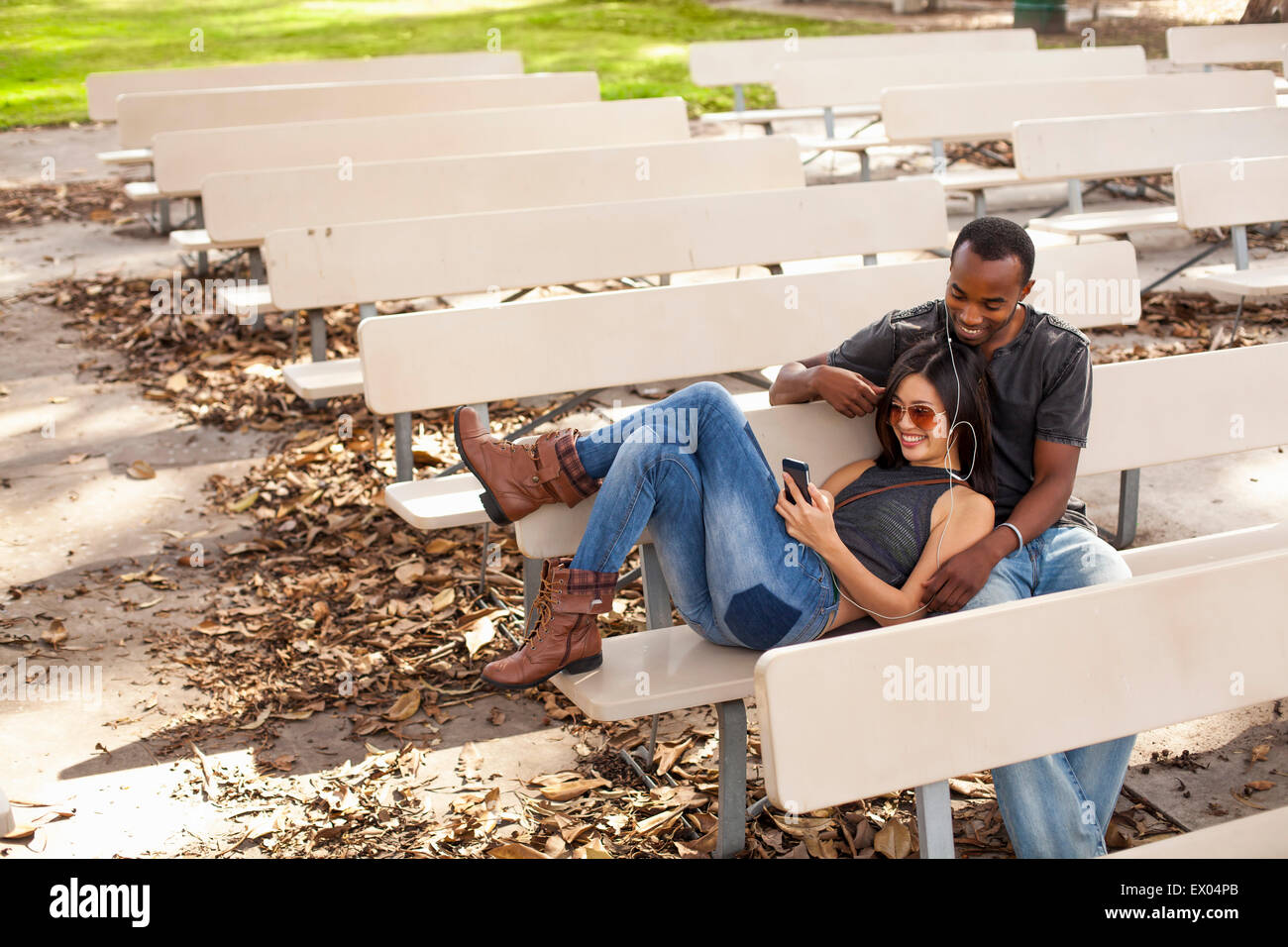Young couple sitting together on bench, sharing earphones Stock Photo ...