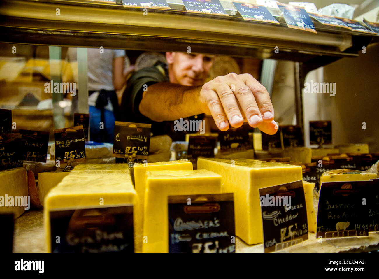 Cheesemonger reaching for cheese in display Stock Photo - Alamy