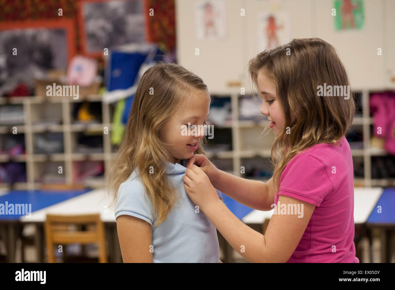 Girl buttoning friend's tee shirt in classroom Stock Photo - Alamy
