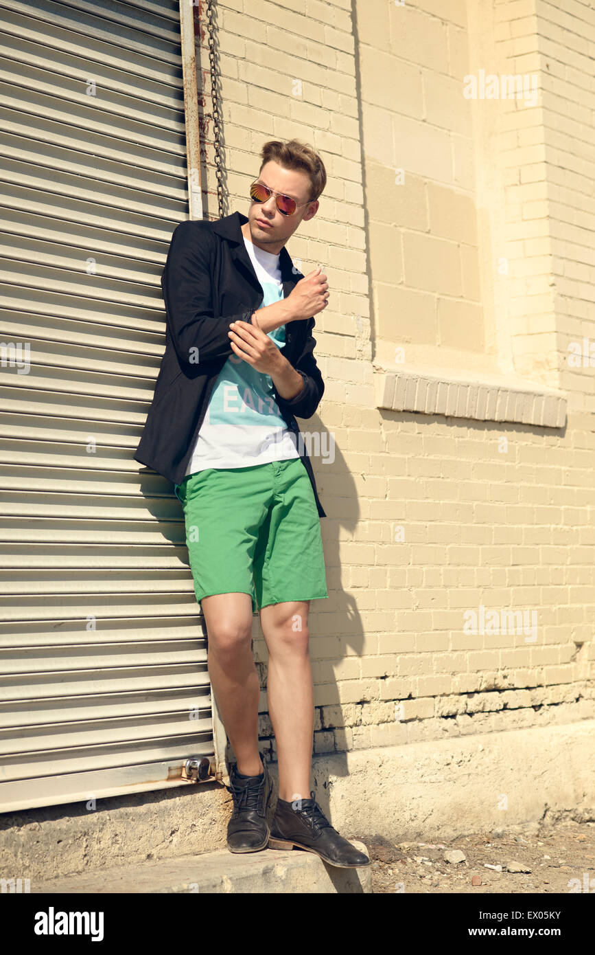 A Caucasian man, male model posing against a light yellow brick wall ...