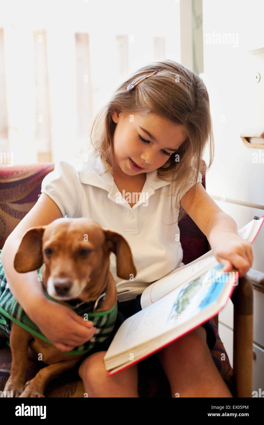 Girl reading book to dog on chair Stock Photo - Alamy
