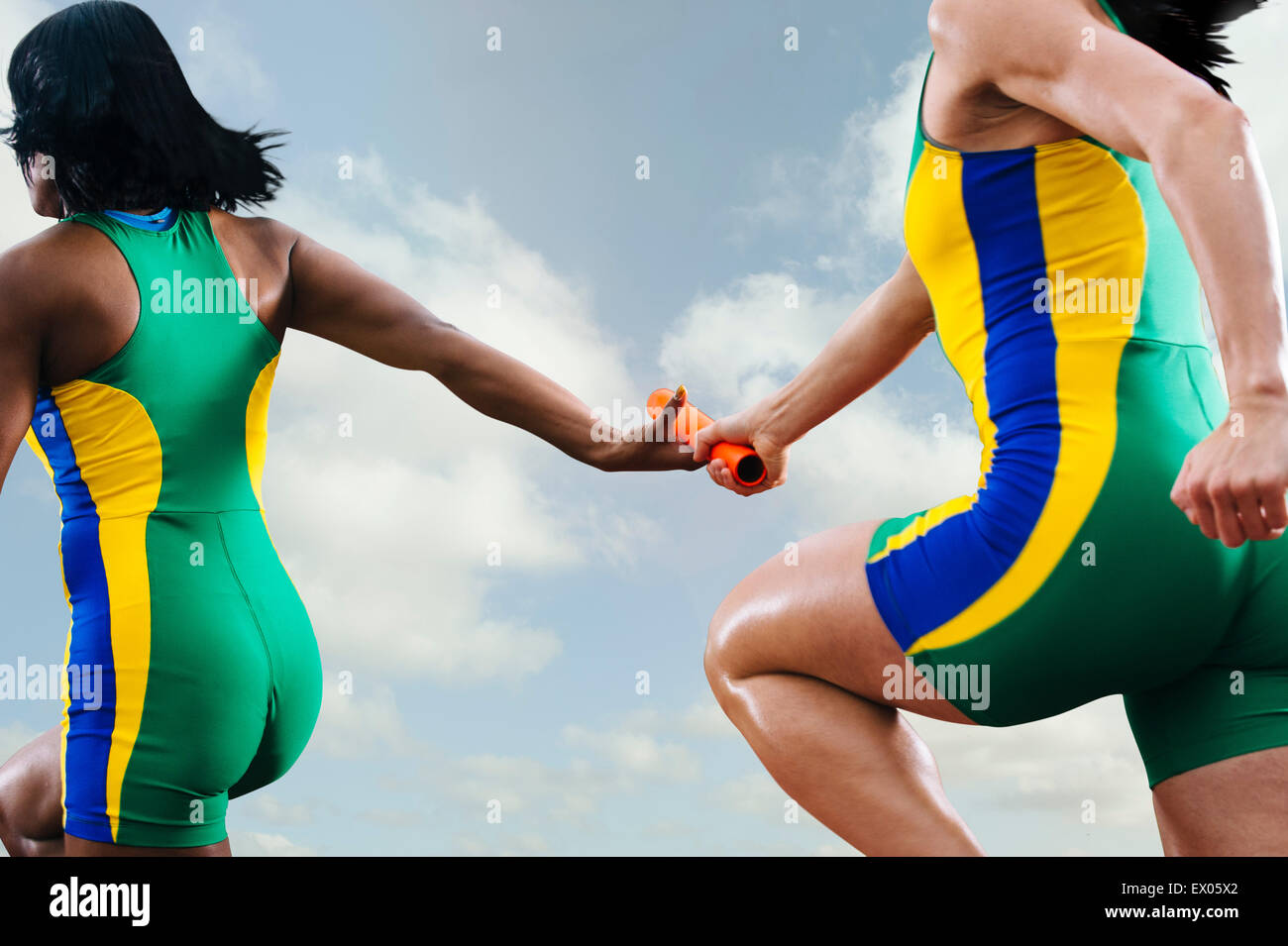 Two female relay athletes exchanging baton whilst running Stock Photo ...