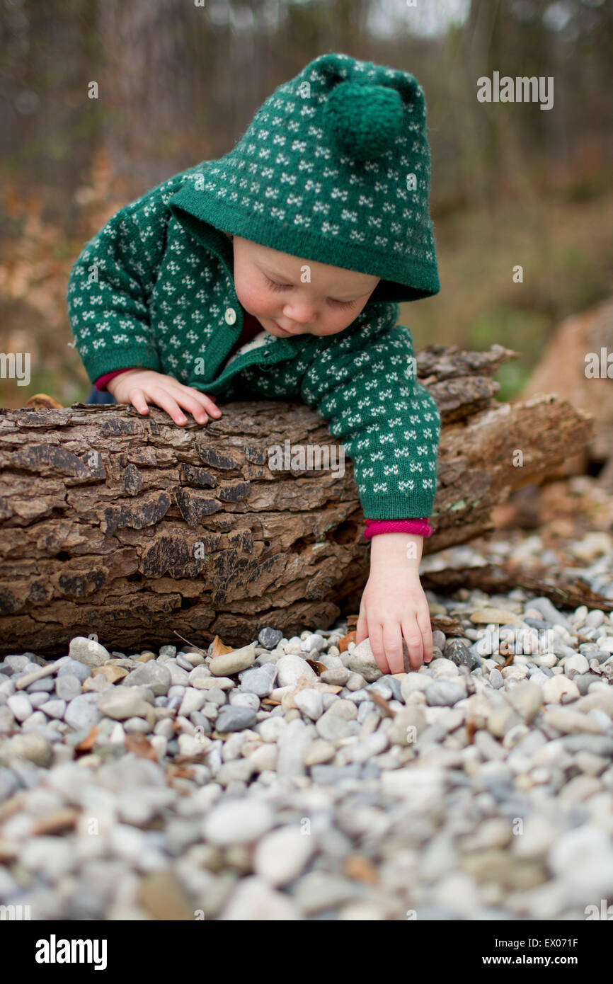 Baby girl leaning over tree trunk and touching pebbles Stock Photo - Alamy