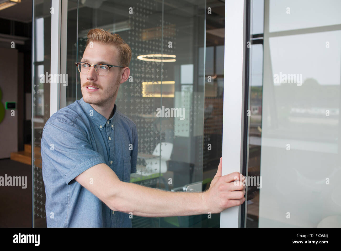 Young man looking over his shoulder from office doorway Stock Photo - Alamy