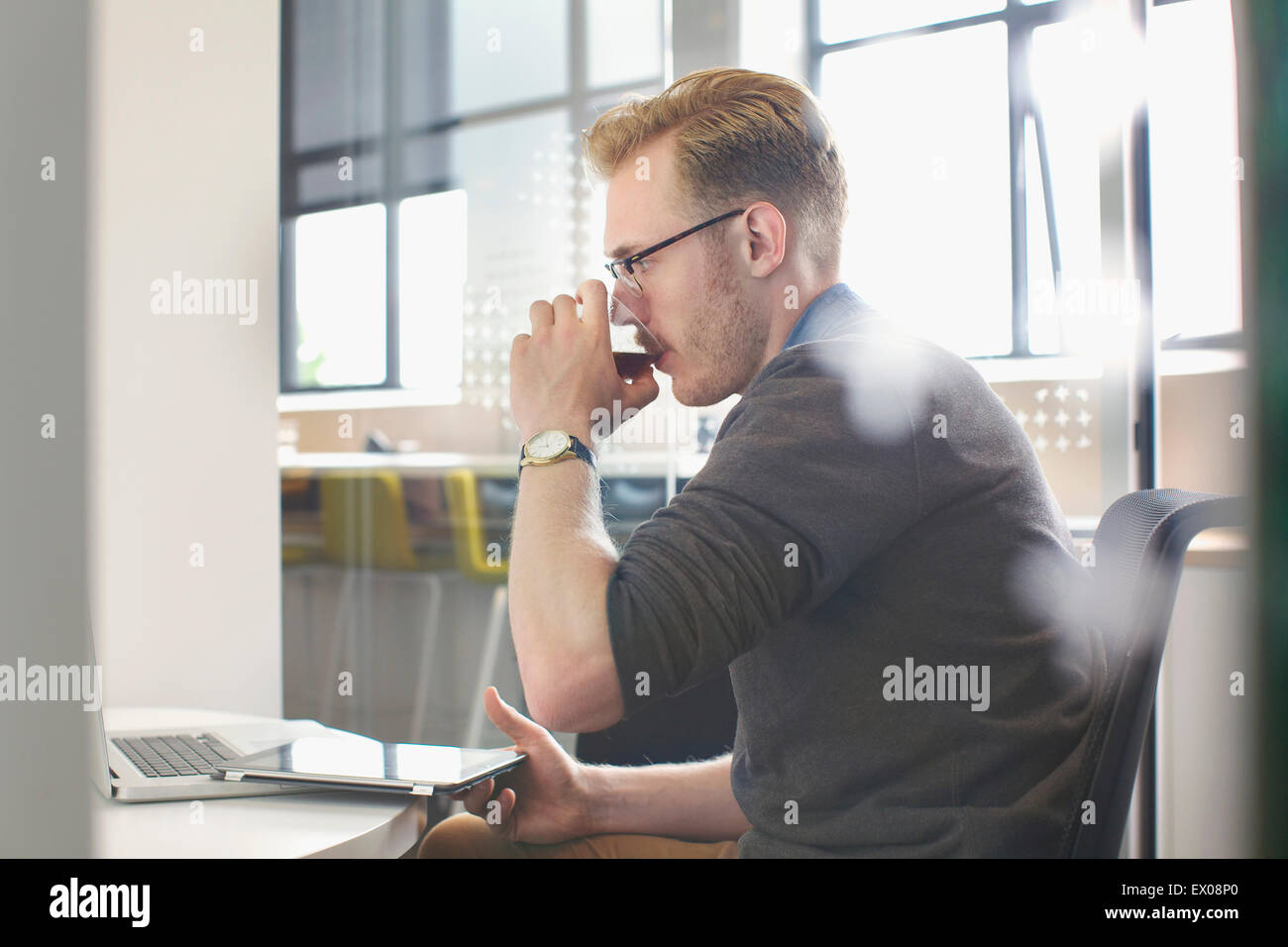 Young man drinking at office desk Stock Photo - Alamy
