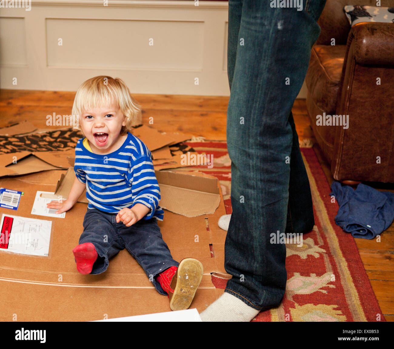 Boy sitting laughing on cardboard box in living room Stock Photo - Alamy