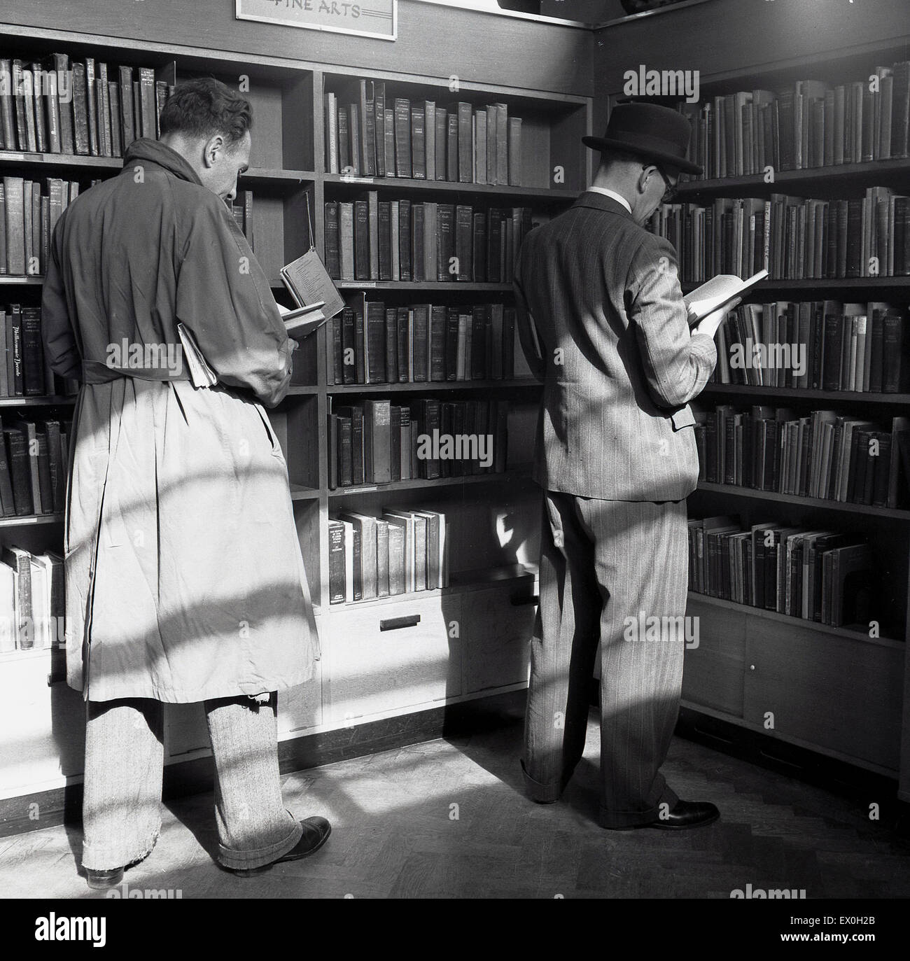 Historical, 1950s, two adult men stand in a corner of a library reading ...