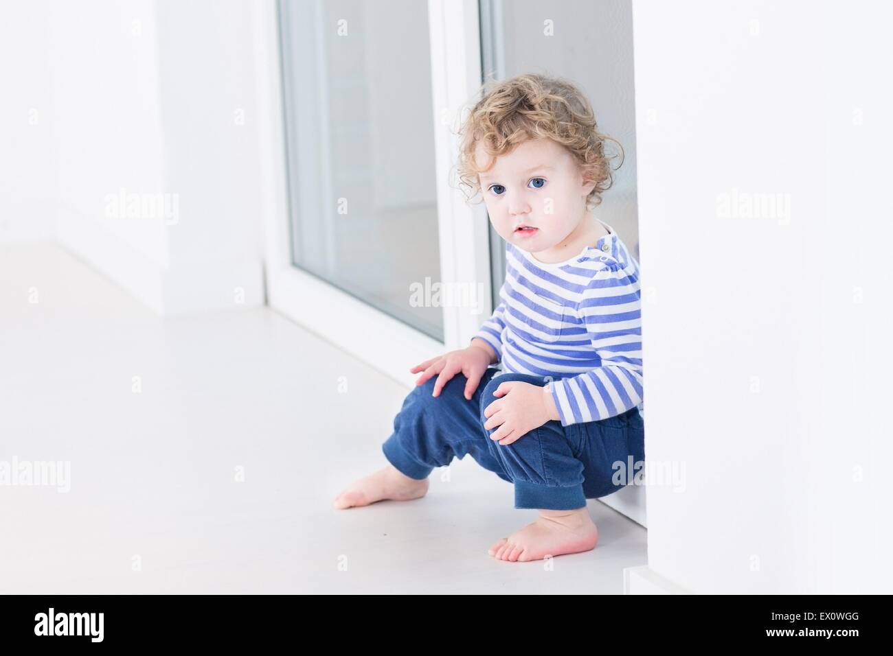 Cute toddler girl sitting at a big window in a white living room Stock ...
