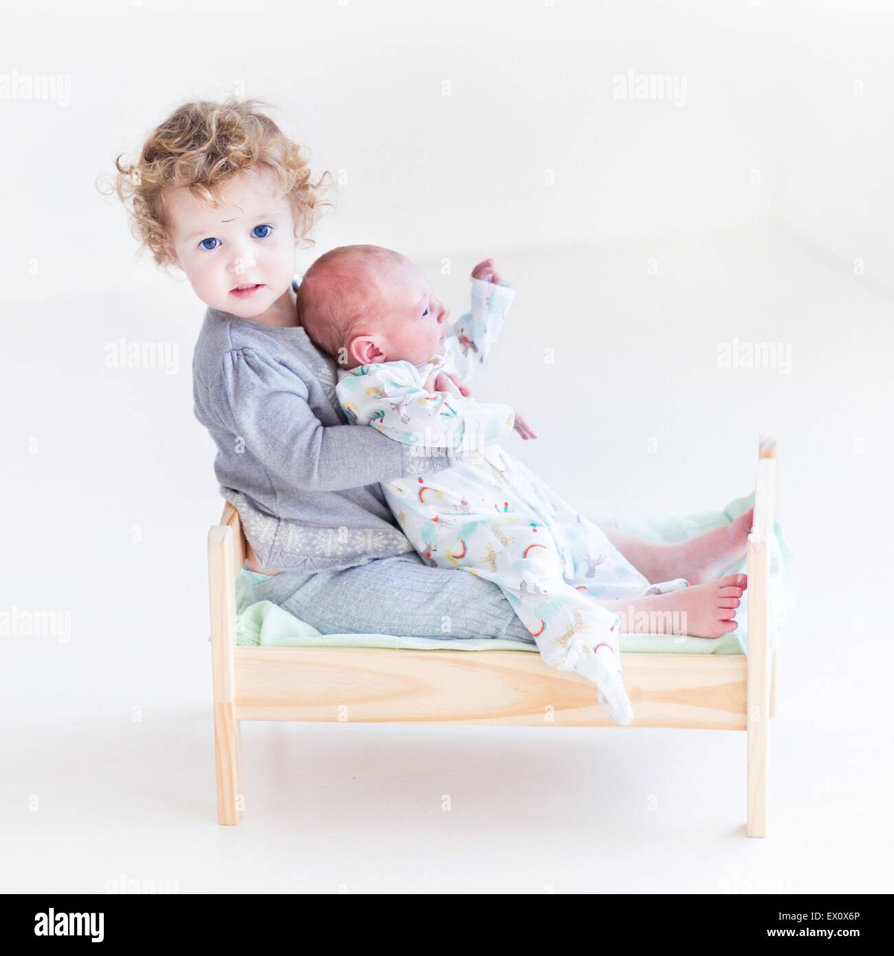Funny toddler girl playing with her newborn baby brother in a toy bed ...