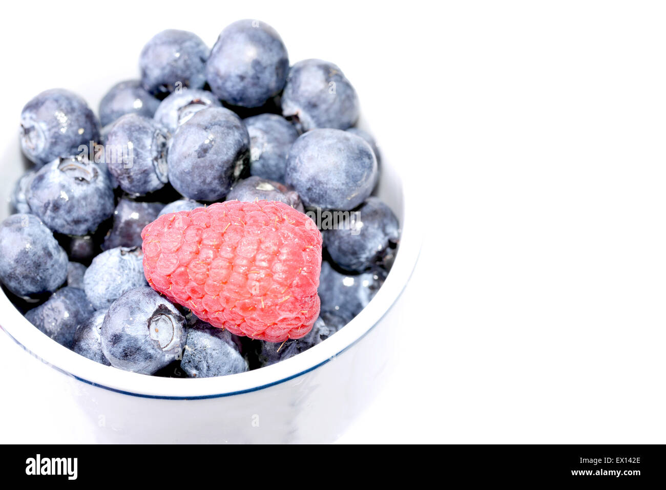 Bowl with a single raspberry over a bunch of blueberries on a white ...
