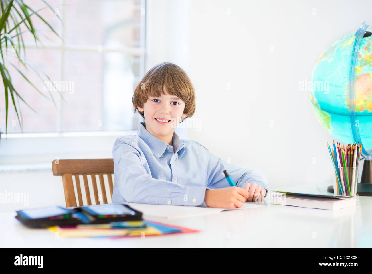 Smiling school boy sitting at a white desk doing his homework Stock ...