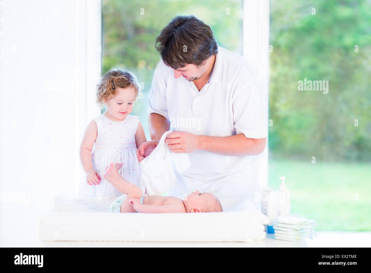 Cute toddler girl helping her father to change a diaper of her newborn ...
