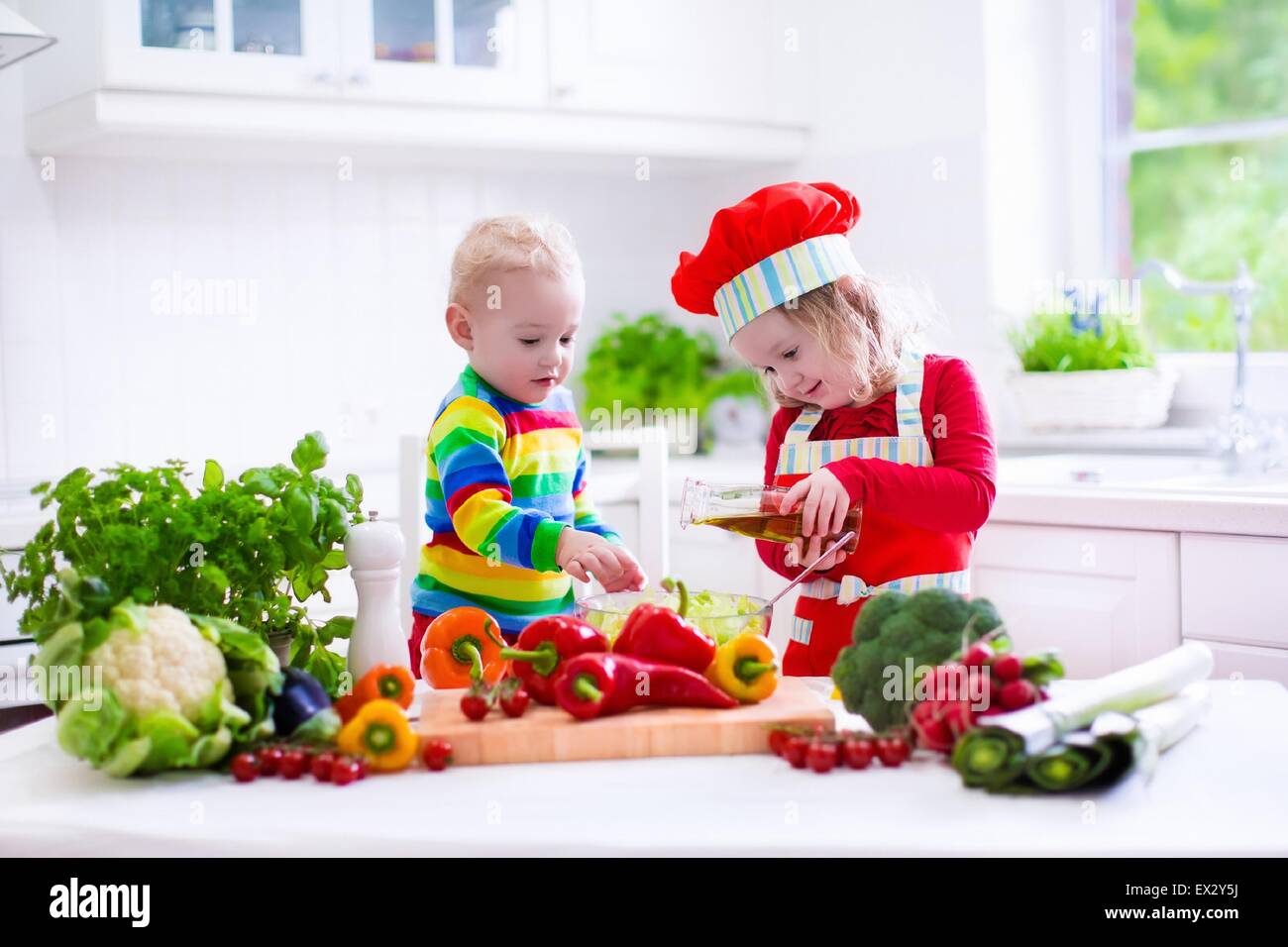 Kids cooking fresh vegetable salad in a white kitchen. Children cook ...