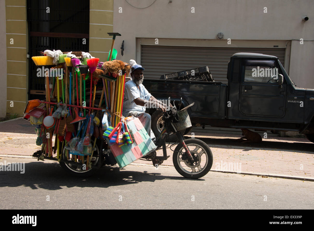 A hawker on his motorcycle, carrying a load of household brooms in ...