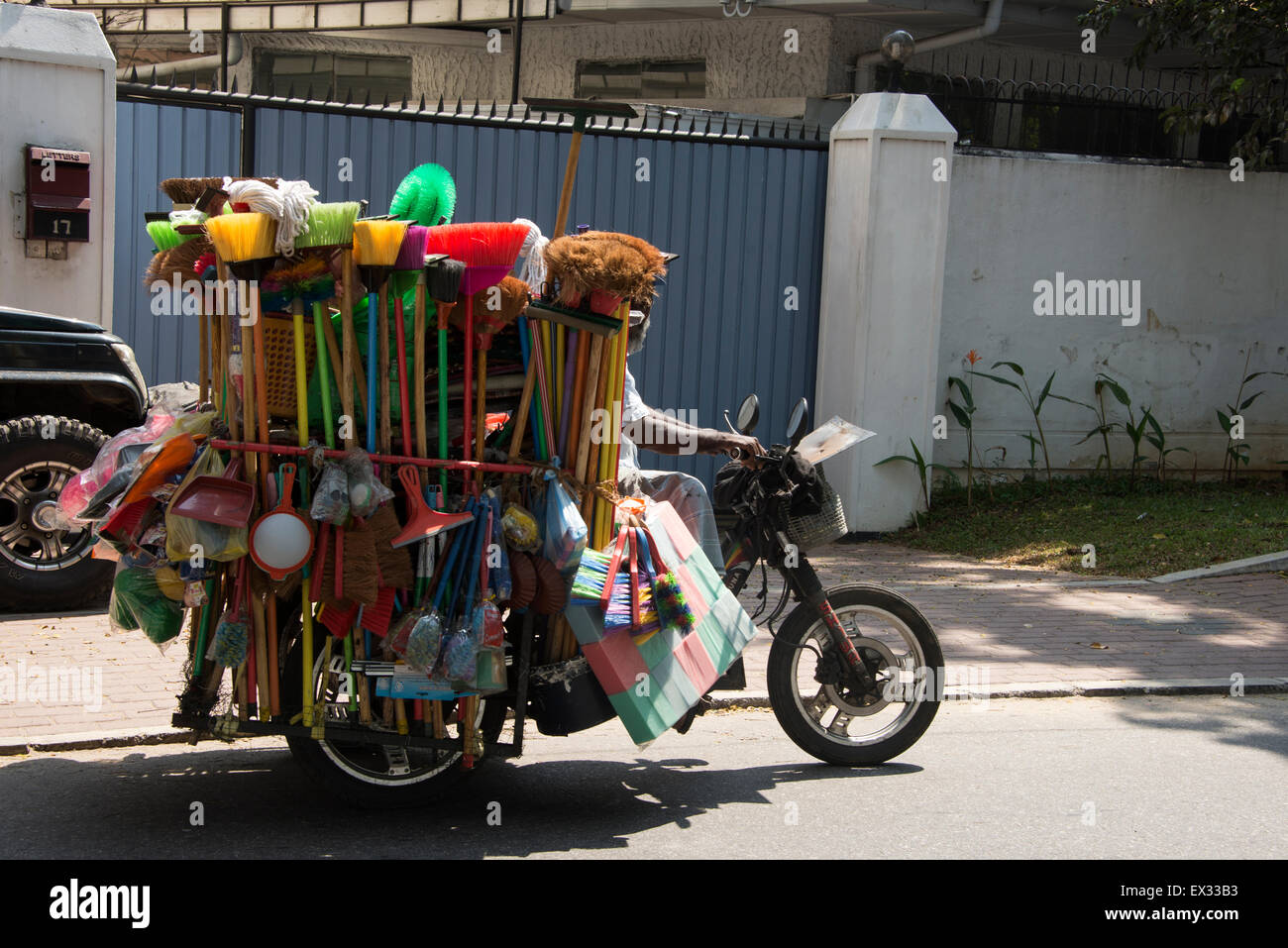 A hawker on his motorcycle, carrying a load of household brooms in ...