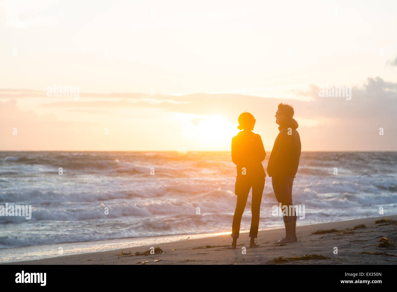 A young couple watch the sun set from the beach in Santa Monica ...