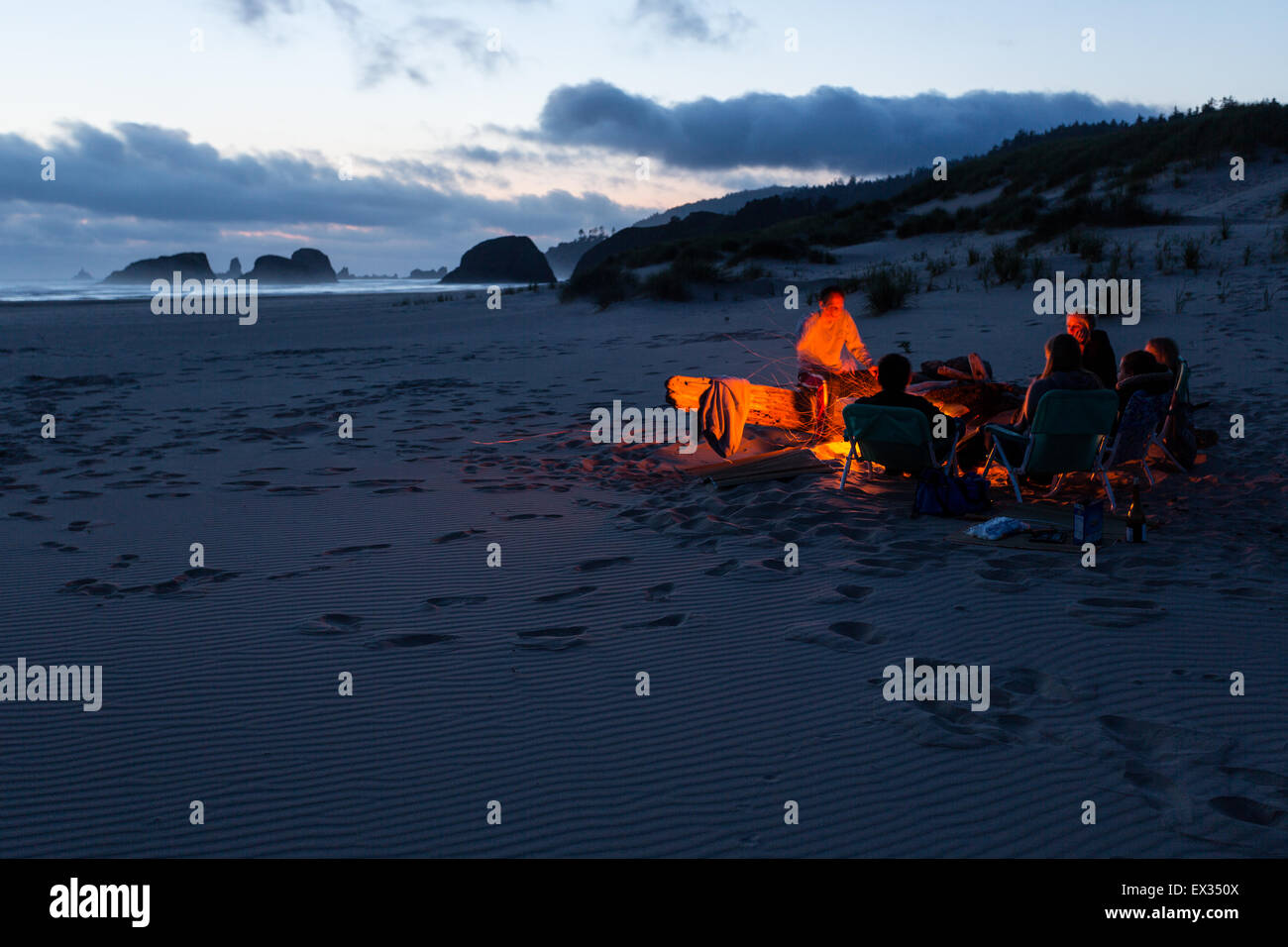 Friends gather around a beach bonfire at dusk in Cannon Beach, Oregon ...