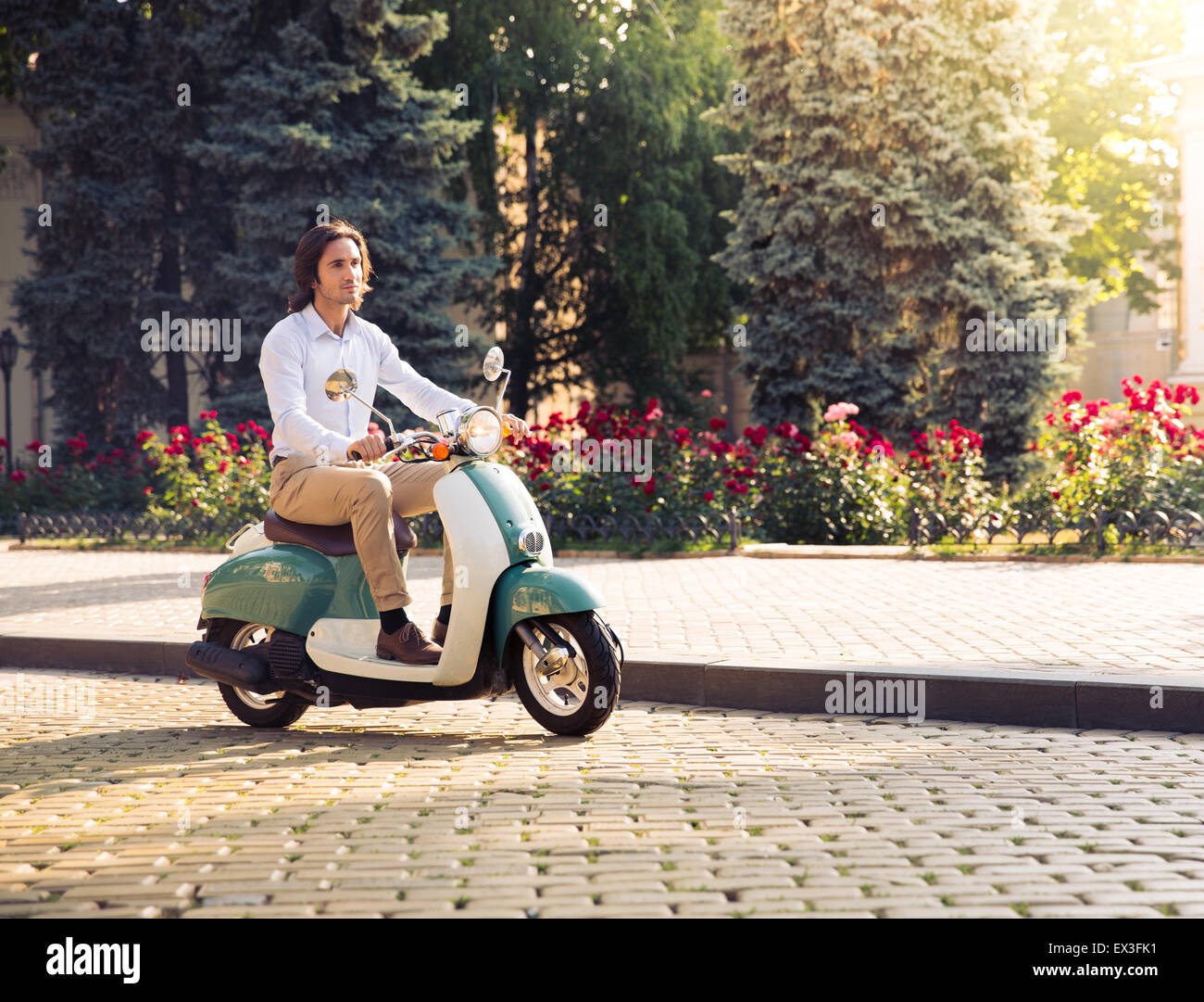 Handsome young man driving scooter in the city park Stock Photo - Alamy