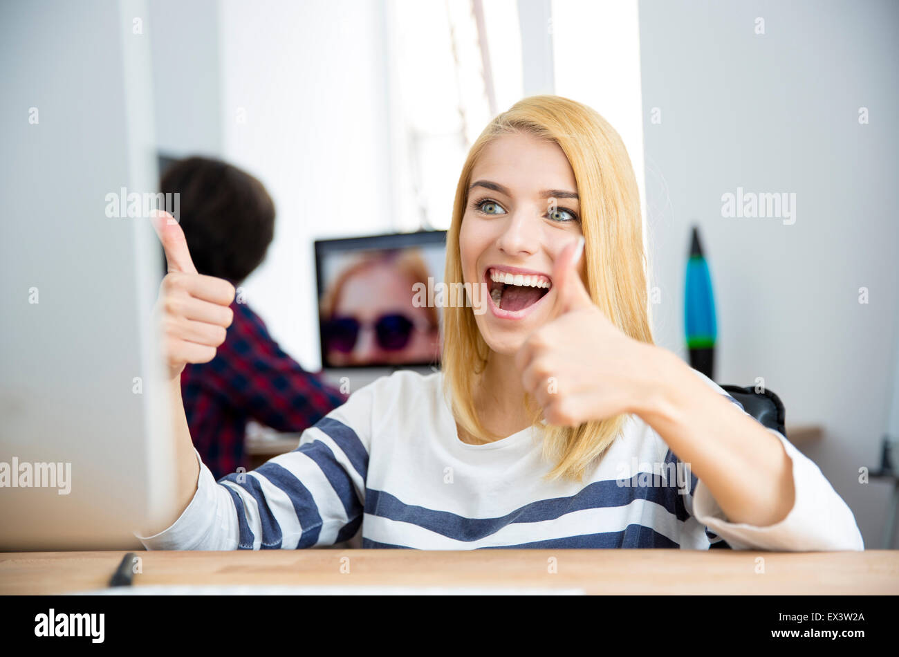 Laughing casual woman showing thumbs up while looking on monitor screen ...