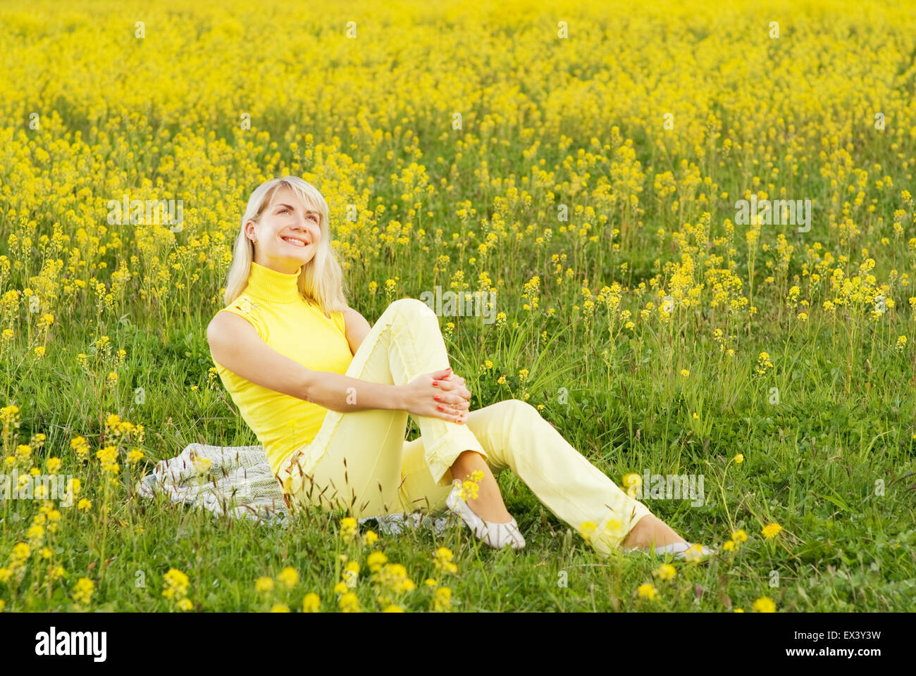 Beautiful young woman sitting in a flower field Stock Photo - Alamy