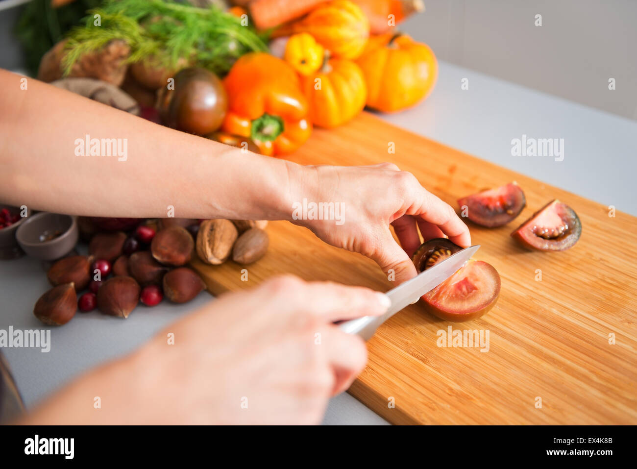 Woman's hand slicing a tomato on a wooden cutting board. In the ...