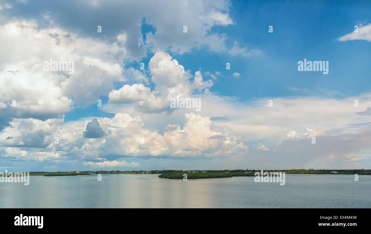 White clouds over a blue sky reflect on the still waters of the lake ...