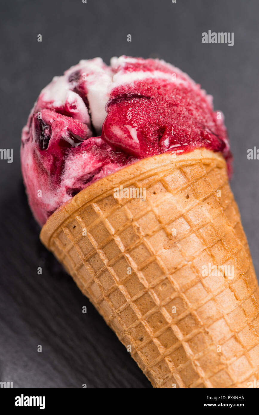 Ice cream cone with scoop of red fruits on dark textured background ...