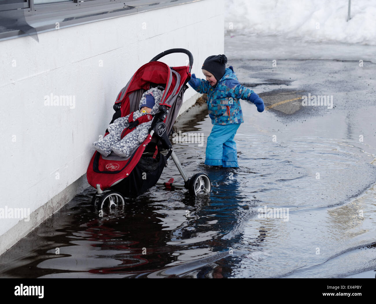 A little boy pushing a his baby sister's pushchair through a deep ...