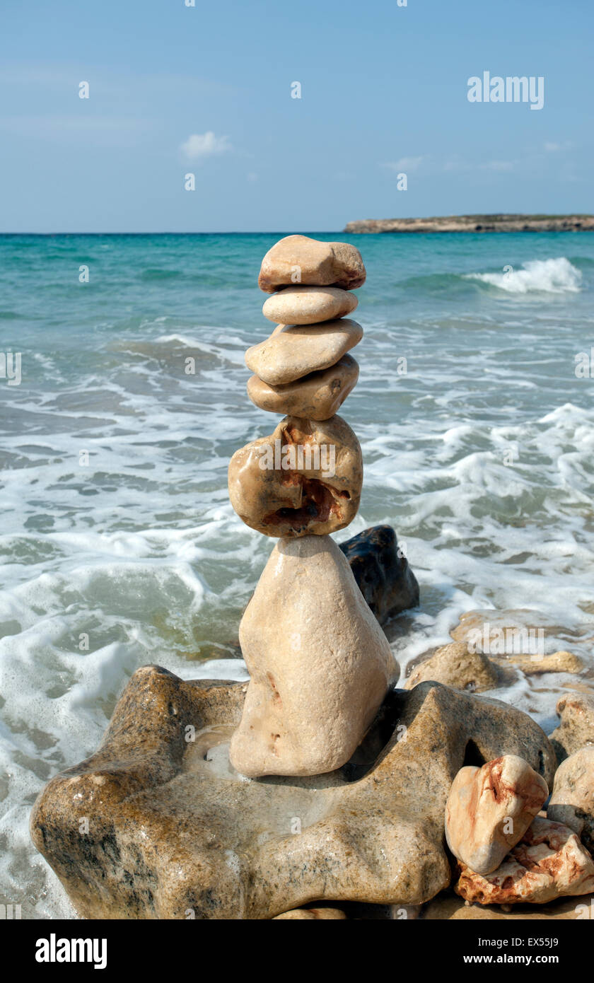 A pile of beach stones made into a sculpture tower on the shoreline of ...