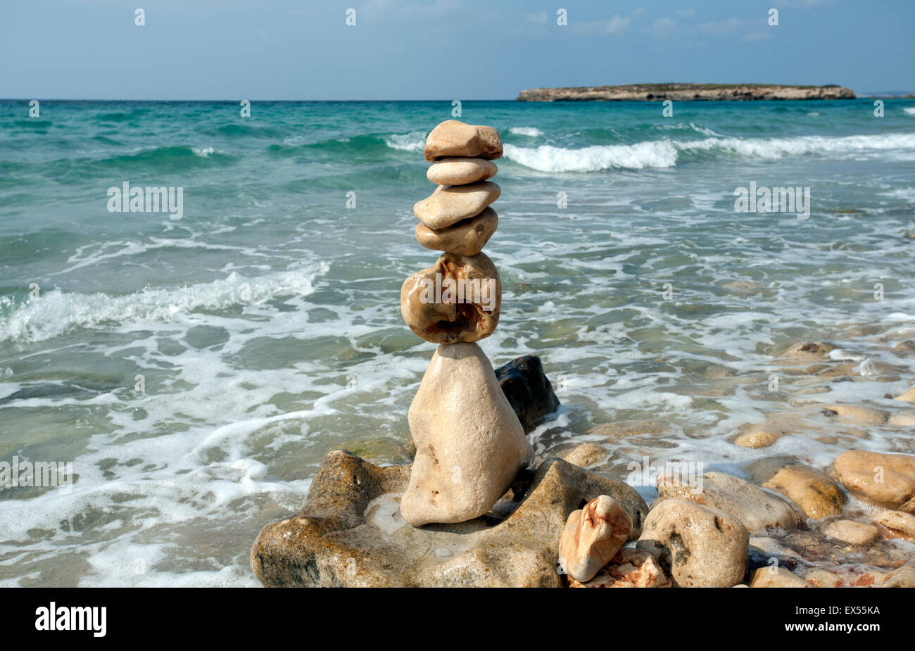 A pile of beach stones made into a sculpture tower on the shoreline of ...