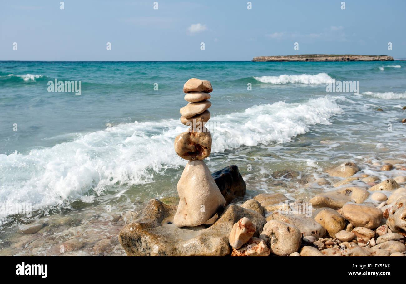 A pile of beach stones made into a sculpture tower on the shoreline of ...