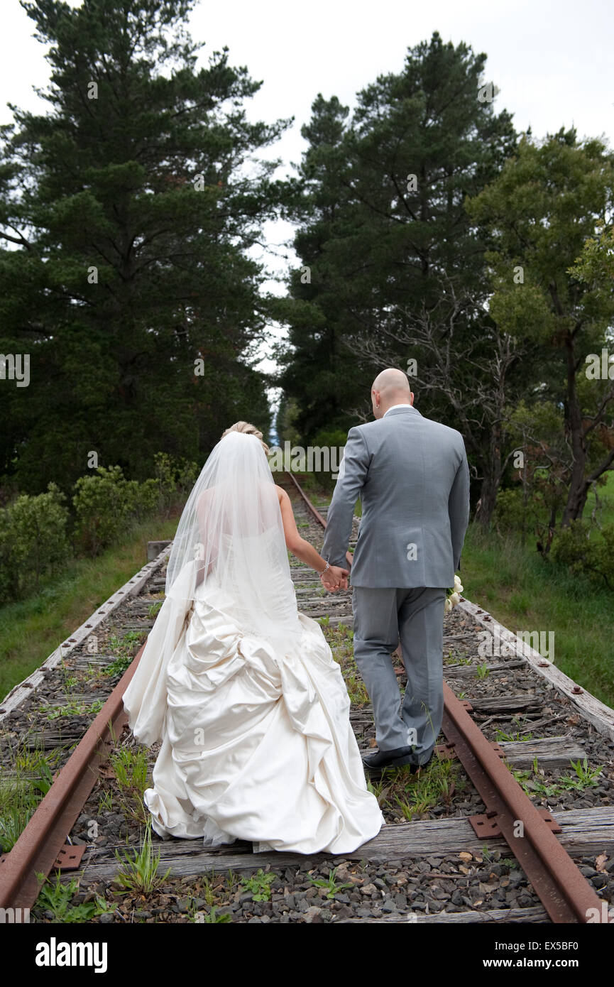 Just married wedding couple walking away holding hands on old rail ...