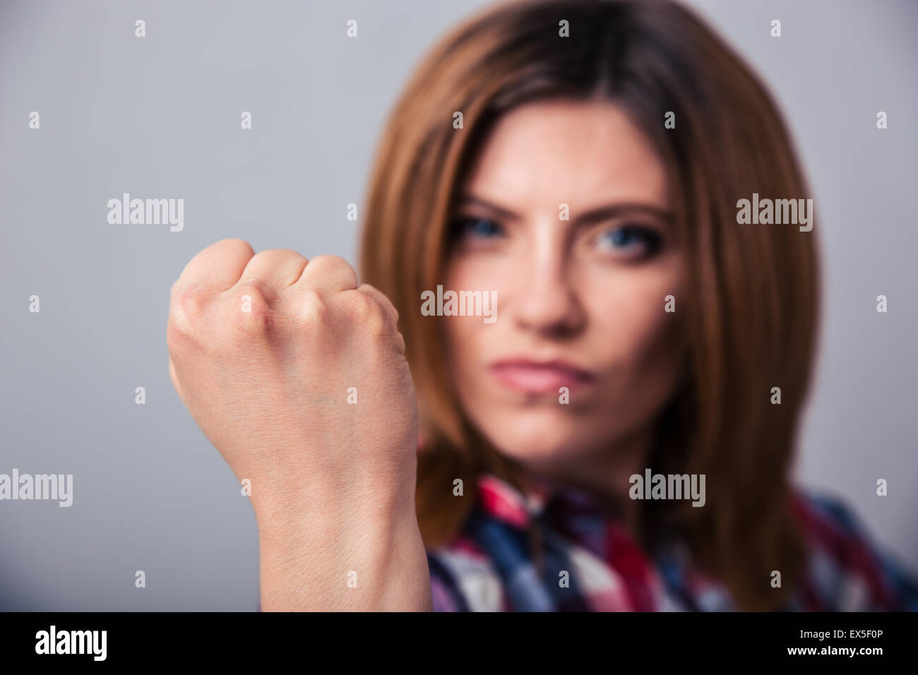 Angry young woman showing fist over gray background. Focus on fist ...