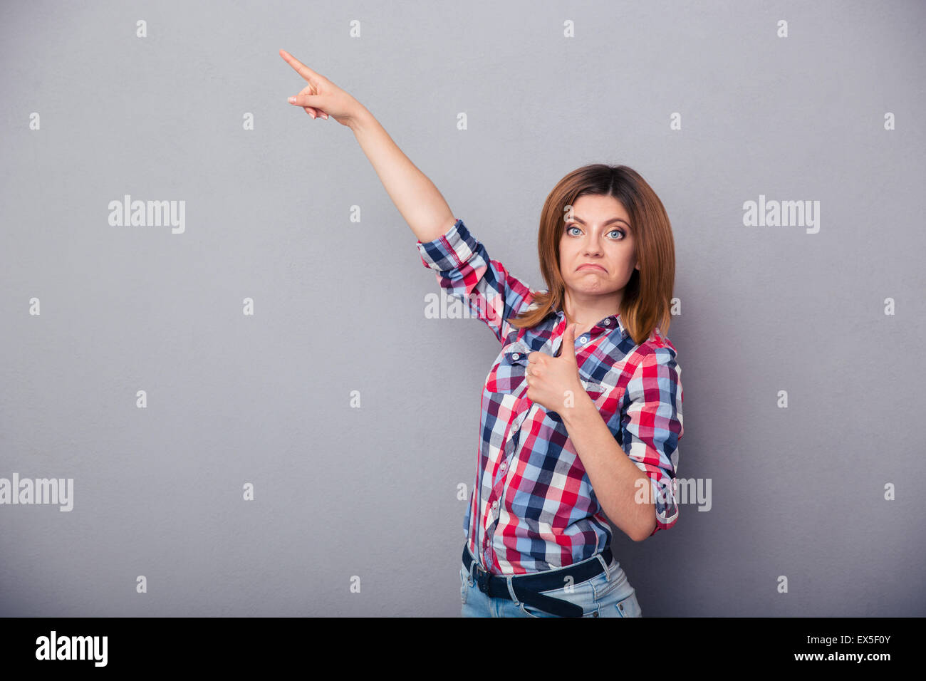 Beautiful young woman showing thumb up and pointing finger up over gray ...