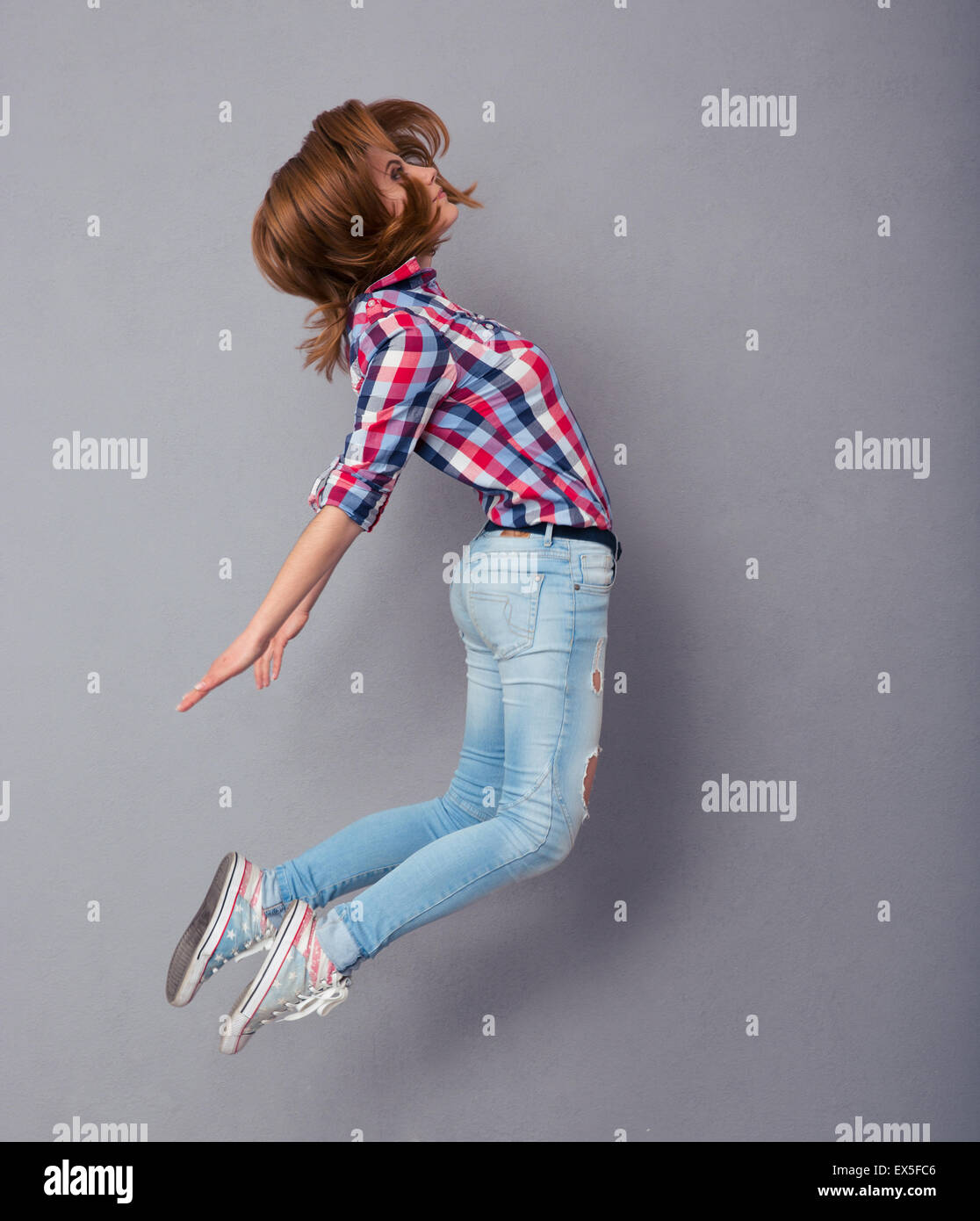 Full length portrait of a young woman jumping over gray background ...
