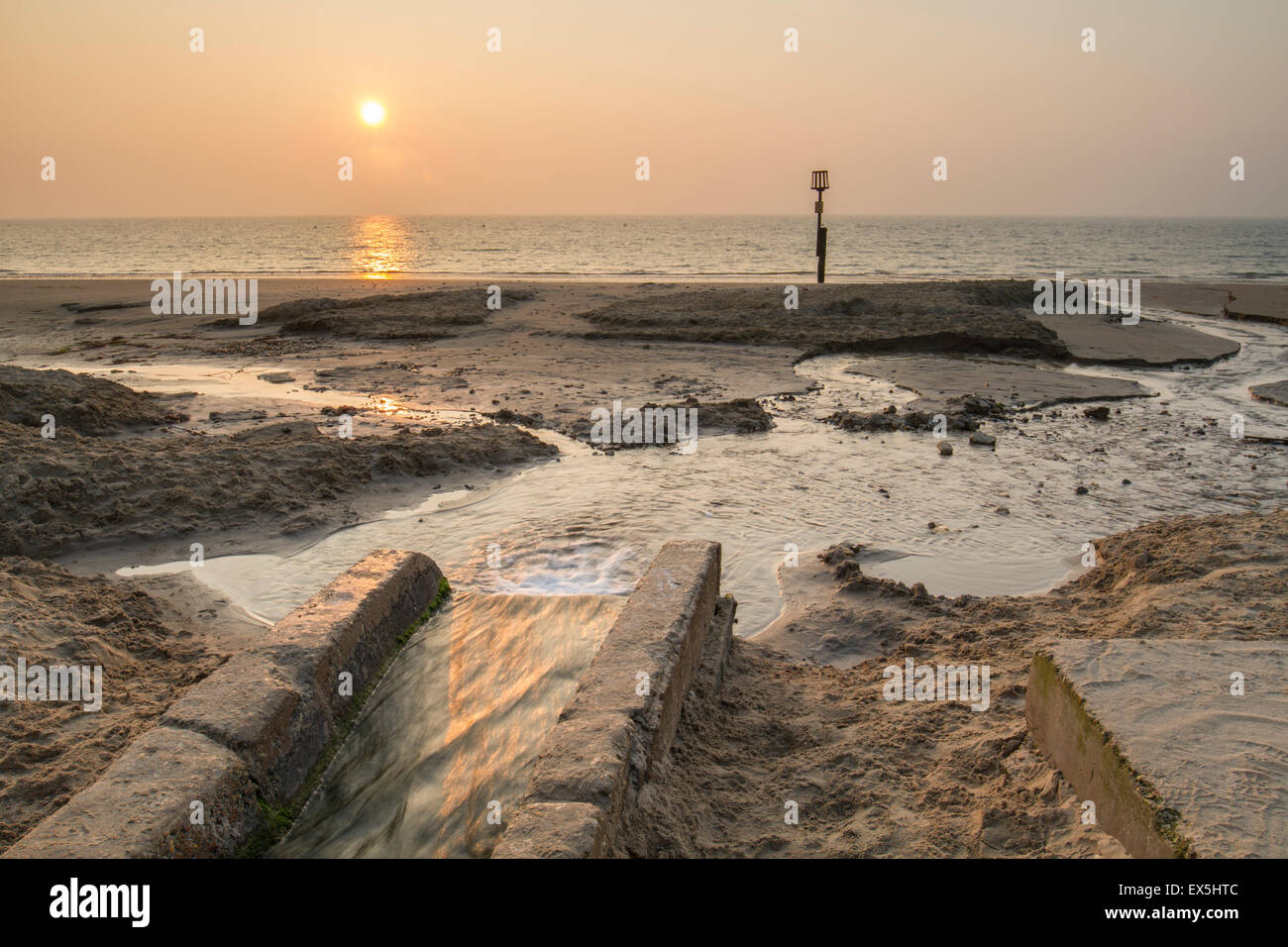 sunrise with block outlet running water onto sandy beach Stock Photo ...