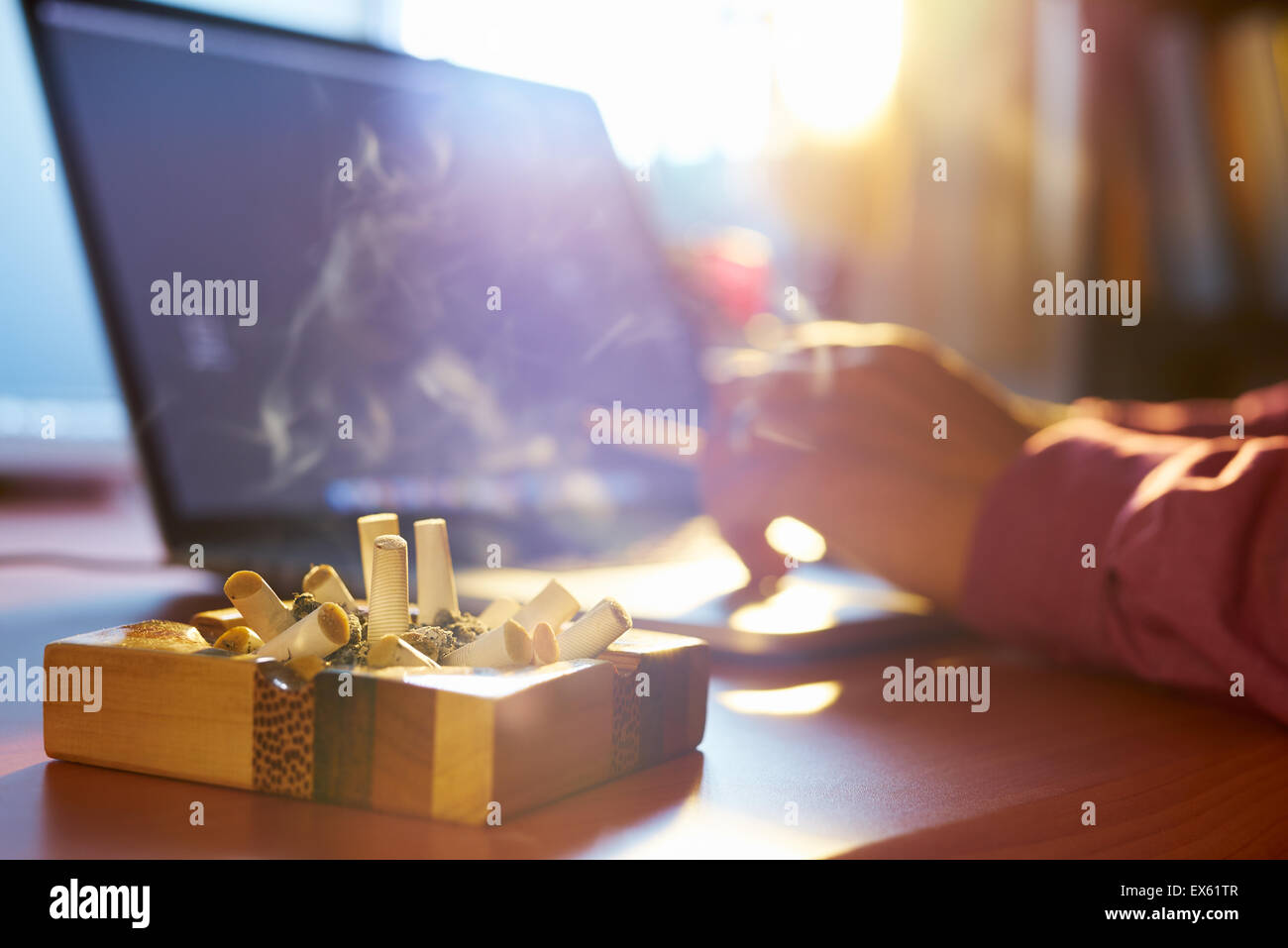Close up of ashtray full of cigarette, with man in background working ...