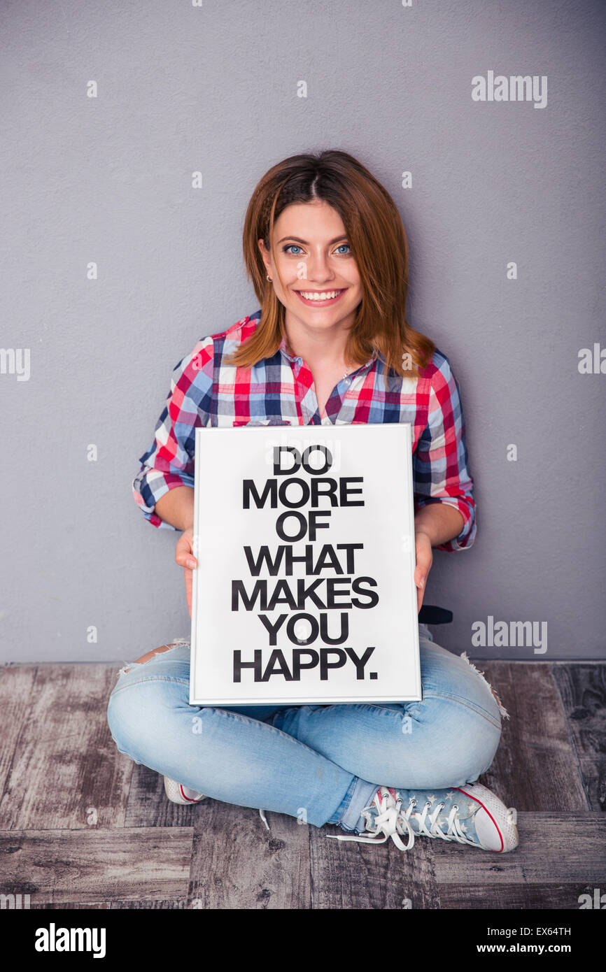 Smiling woman sitting on the floor and holding board with motivational ...