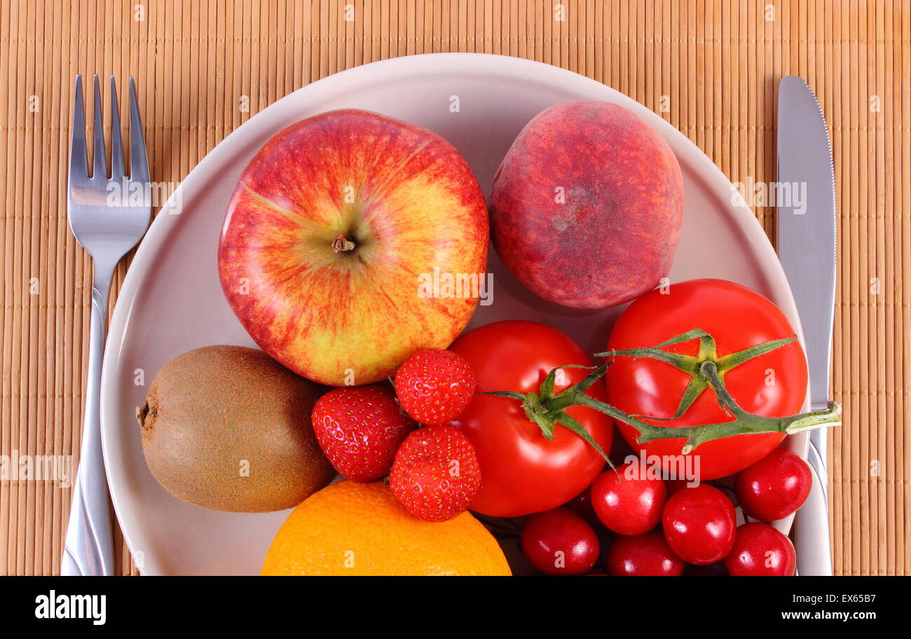 Fresh ripe fruits and vegetables lying on plate and cutlery on wooden ...