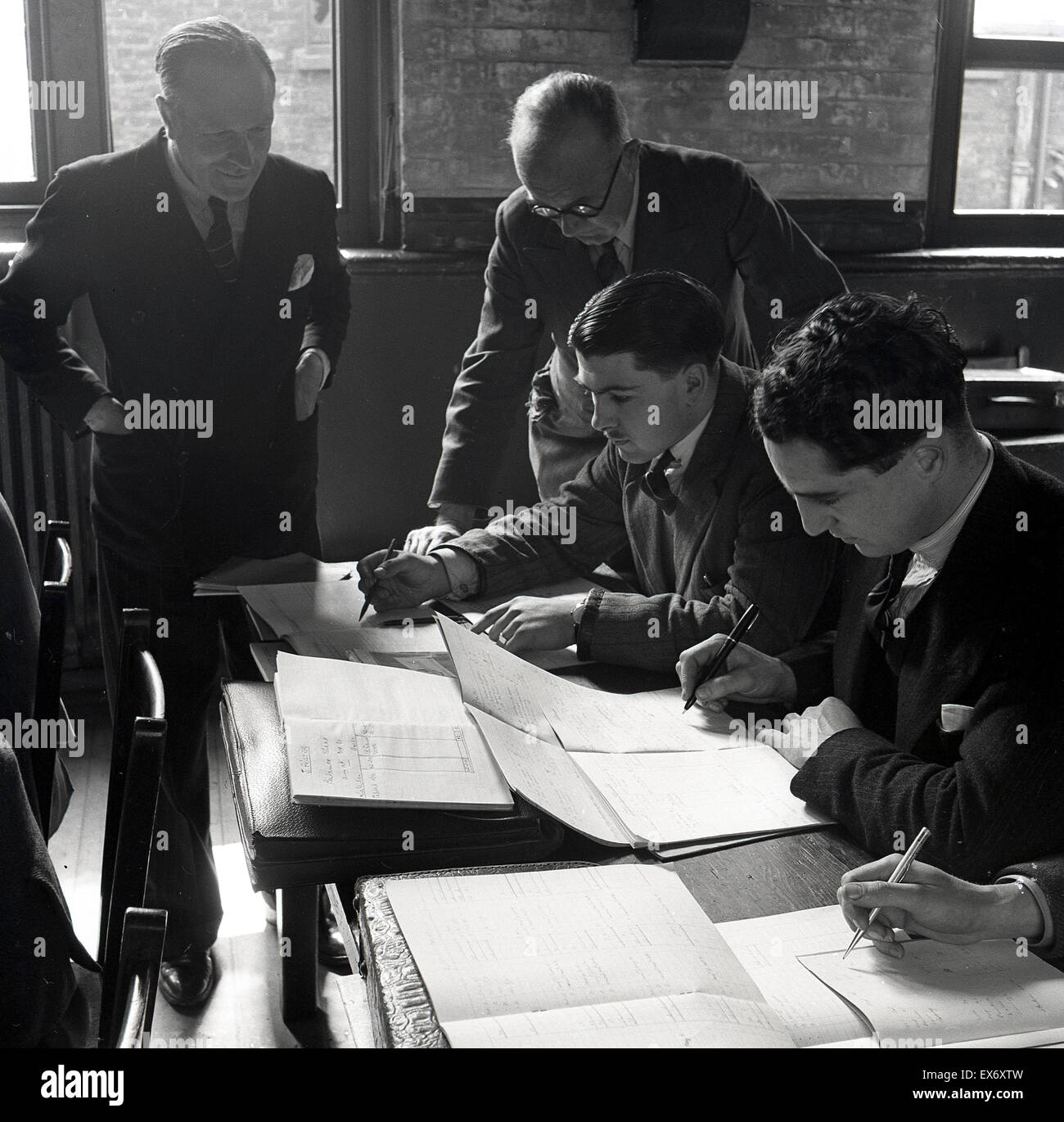 1950s, historical, a group of suited men examine or study a number of ...