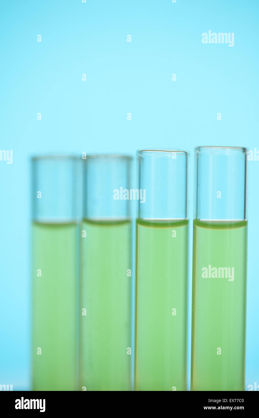 row of testtubes filled with pale green liquid against blue background ...