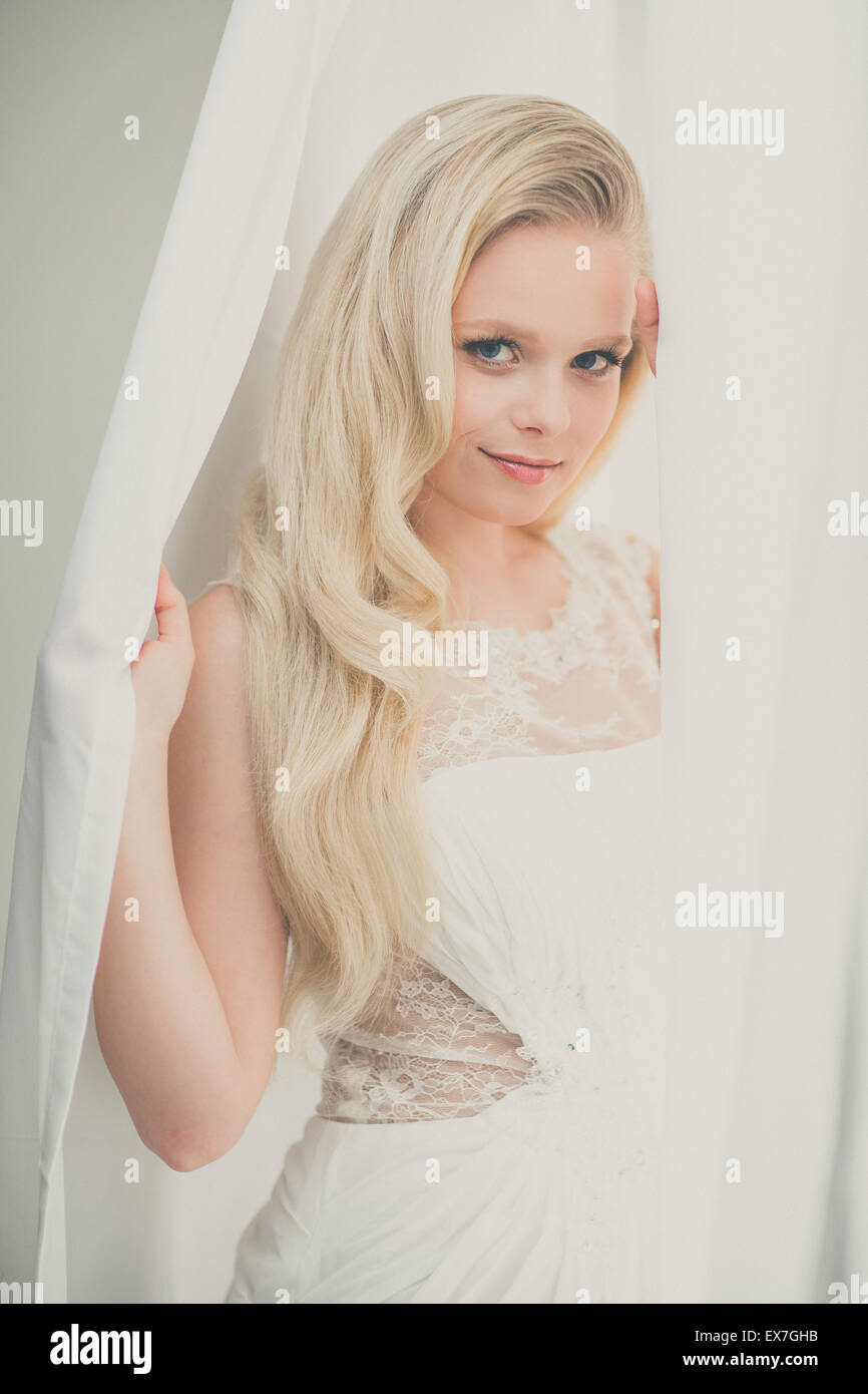 Gorgeous young woman/bride wearing a lovely dress, in a window, hiding ...